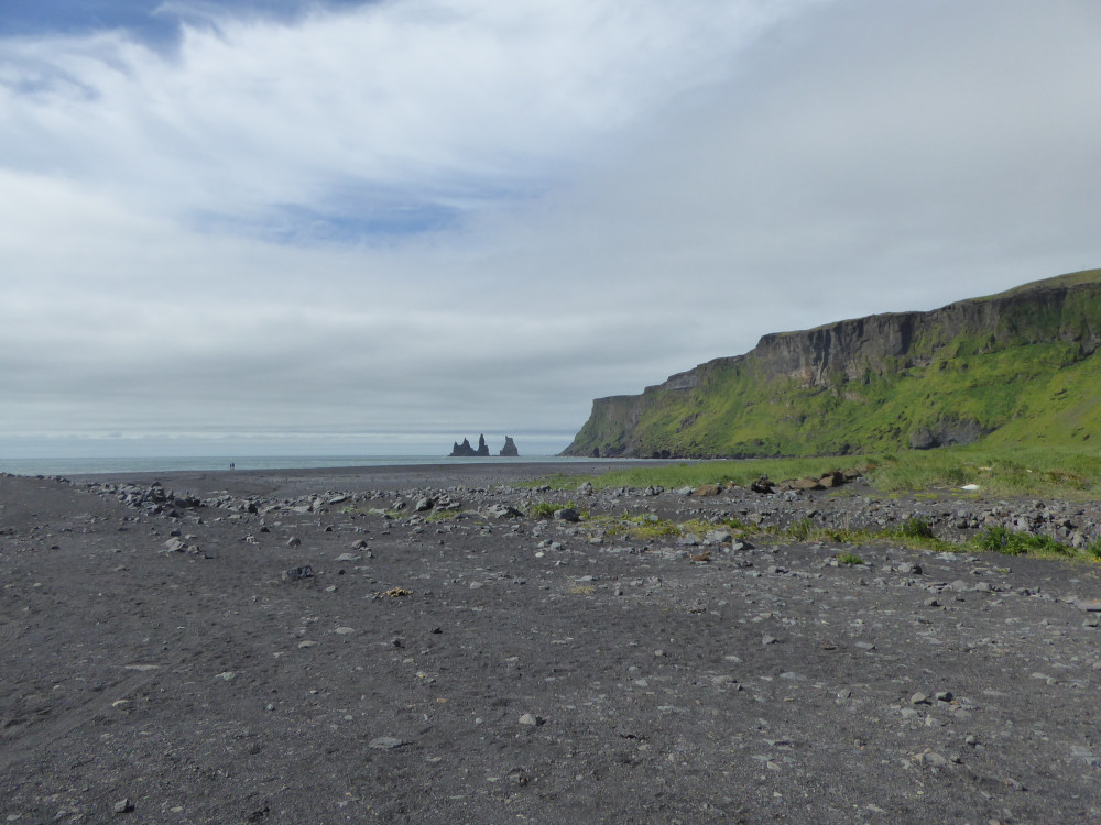 The grey sand beach at Vik, with a green mossy mountain descending into ...
