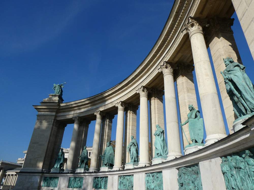 A curved stone monument of many columns. Between the columns are blue ...